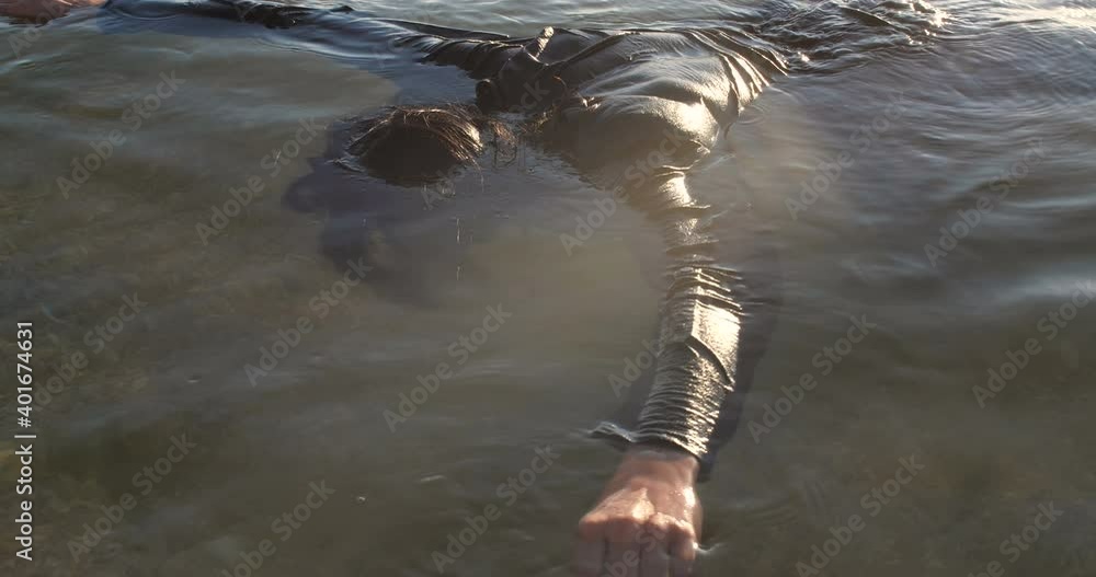 Drowned man with long dark hair in the water sways in the muddy water ...