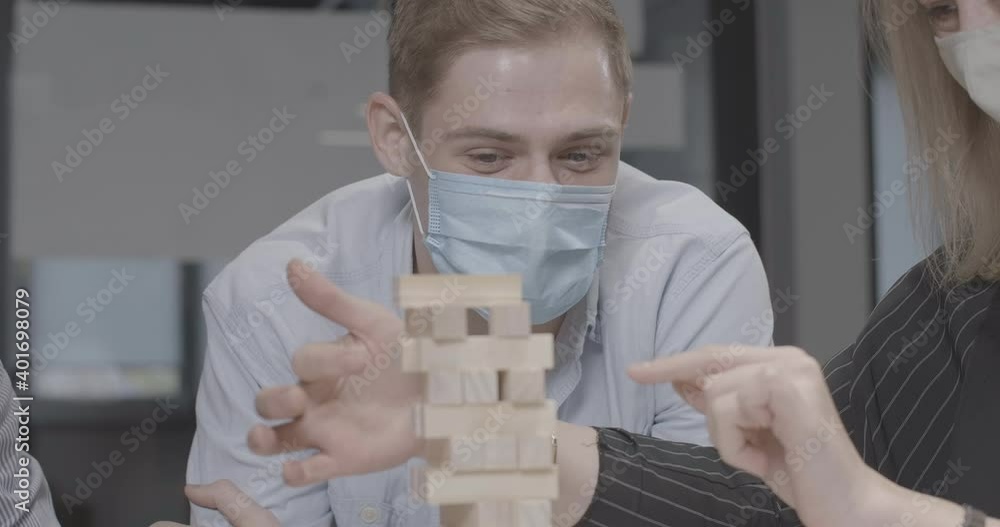 Group of positive friends in Covid-19 face masks playing Jenga game ...
