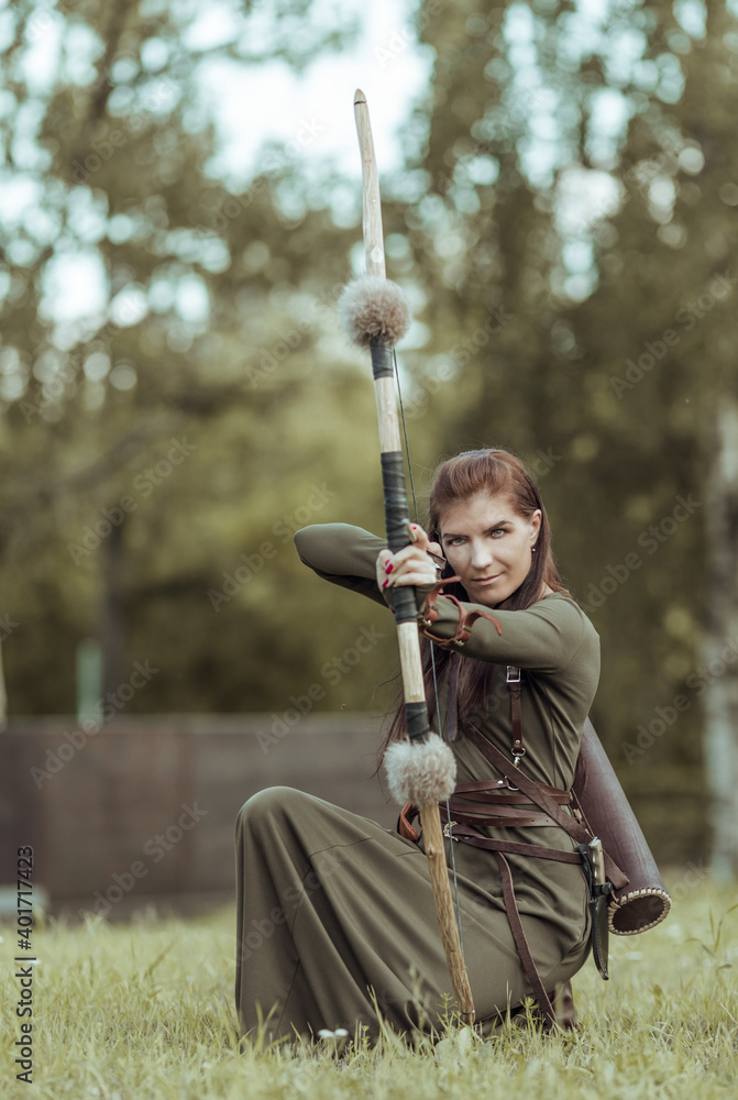 Medieval woman warrior with a bow sits in a clearing and aims from a ...