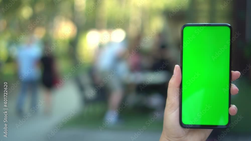 Close up hands woman holding phone with vertical green screen on busy street background pavement ...