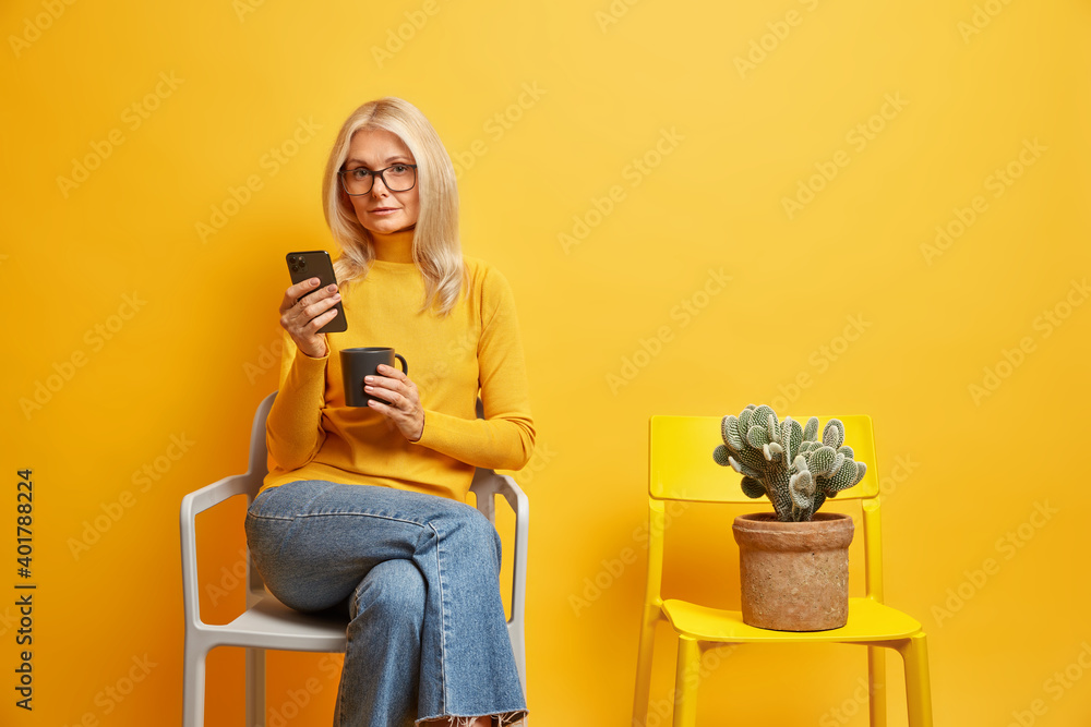 Calm serious woman with blonde hair uses modern gadget for texting ...