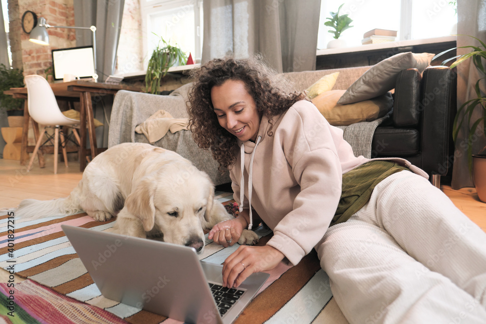 Young woman lying on the floor with her dog and using laptop computer ...