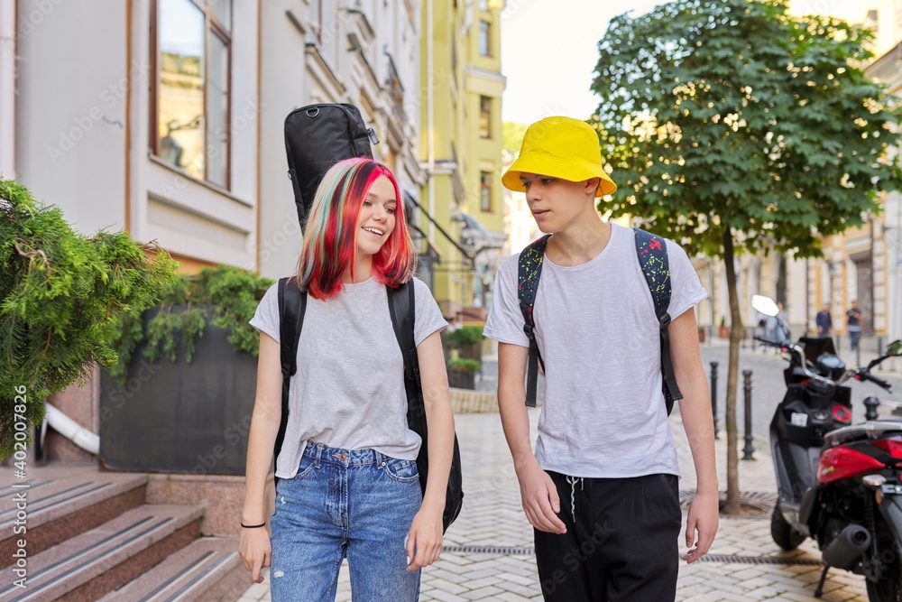 Creative teenagers guy and girl walking and talking along city street ...