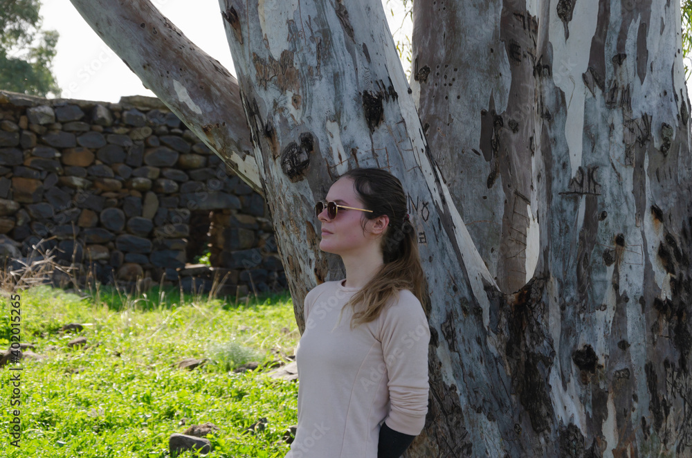 girl model in sunglasses posing standing with her back to a large tree ...
