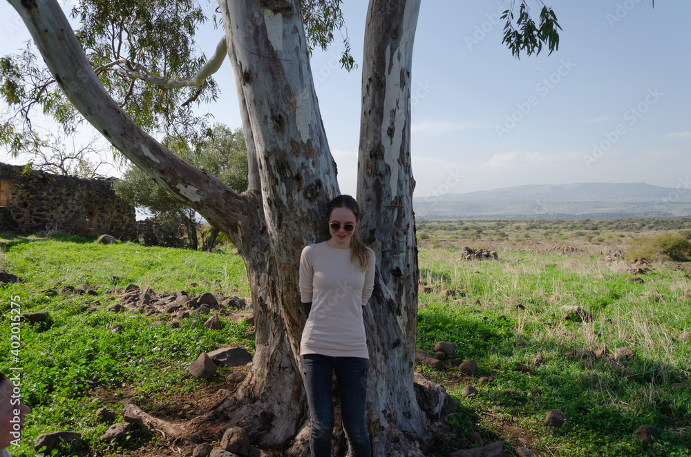 girl model in sunglasses posing standing with her back to a large tree ...