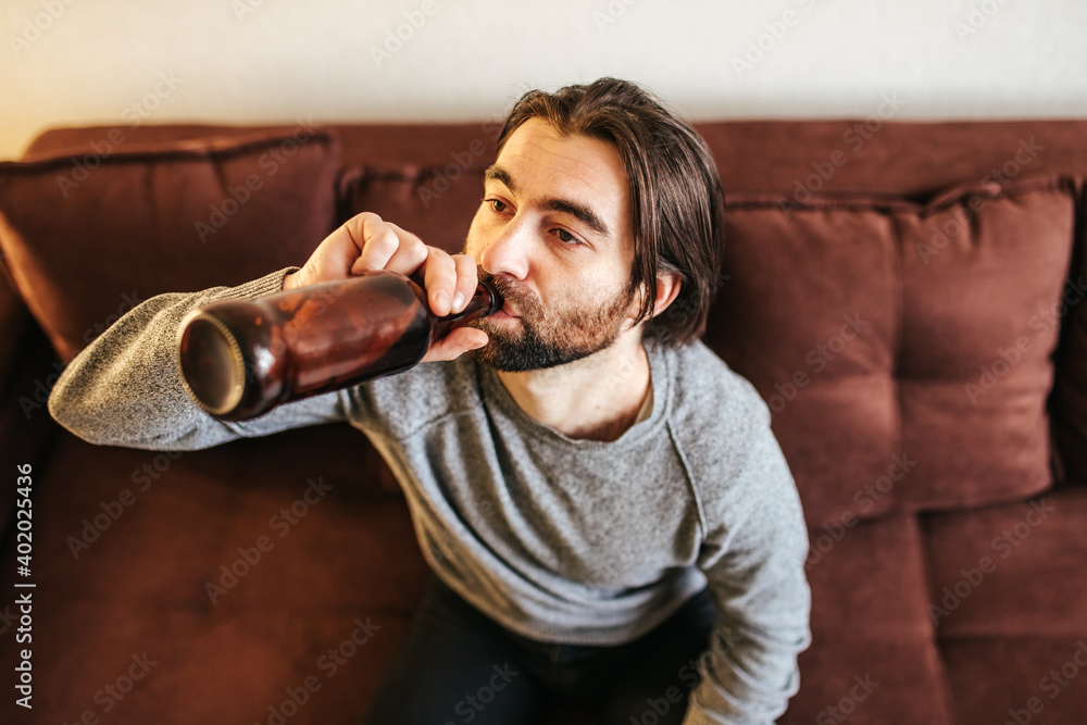 top view of young depressed drunk man drinking beer from the bottle, at ...