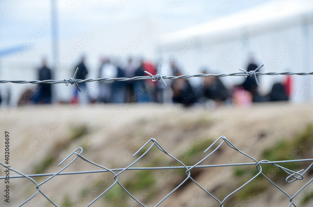 Barbed wire in refugee camp. Migrants behind chain link fence in camp ...
