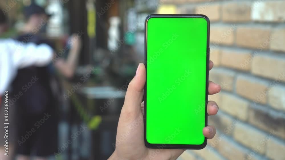 Close up hands woman holding phone with vertical green screen on busy street background pavement ...