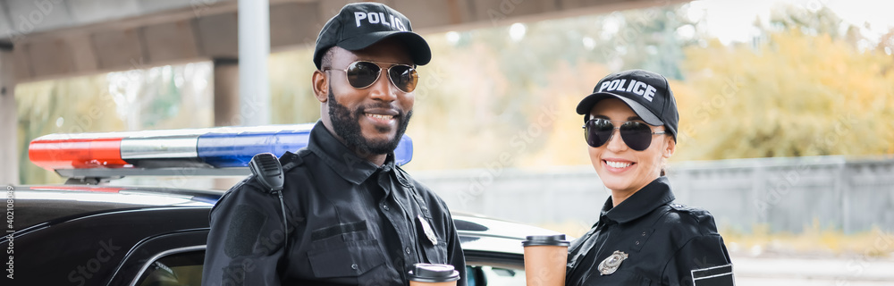 happy multicultural police officers with paper cups looking at camera ...