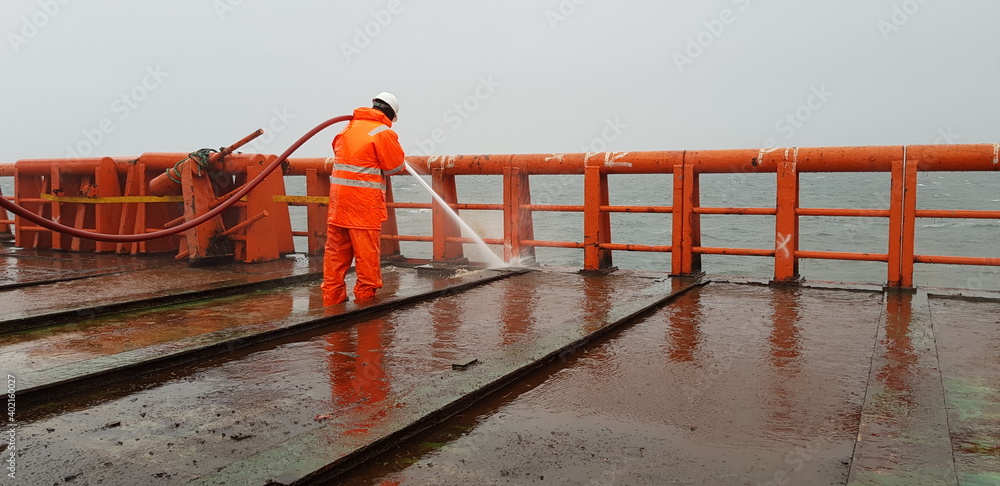 a sailor washes the deck of a ship with the pressure of sea water from ...