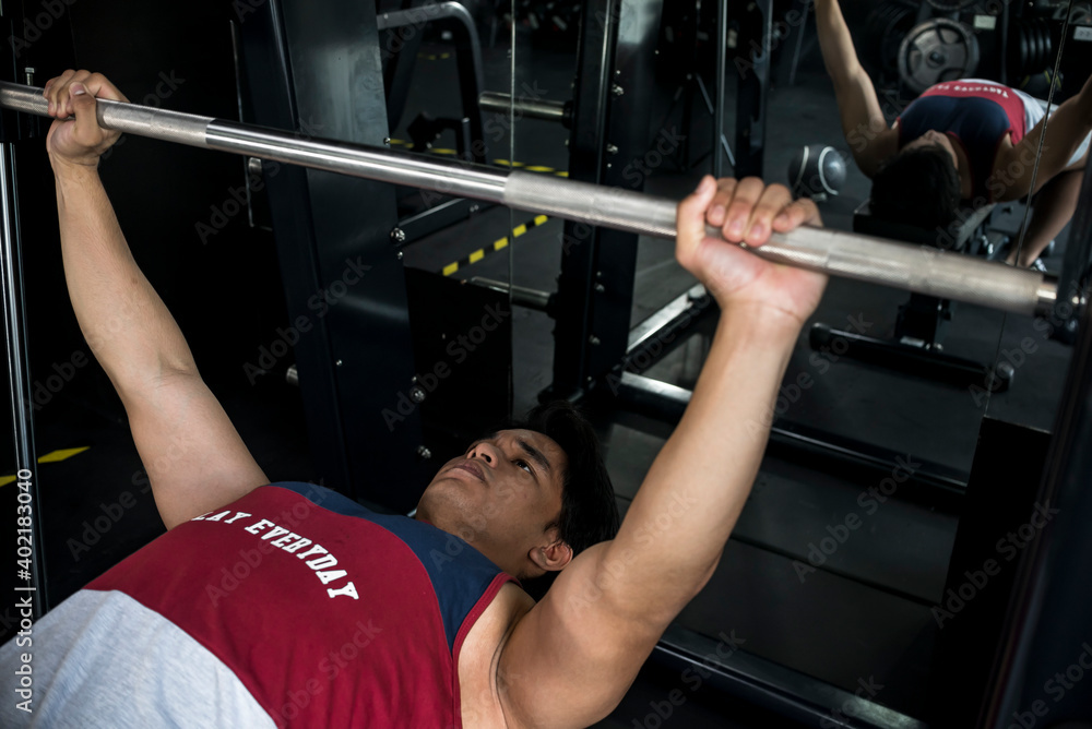 A young asian man does flat barbell bench presses on the smith machine ...
