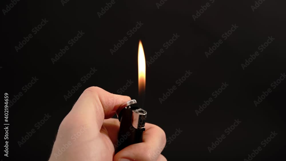 Ignition of a lighter on black background with a hand and let the fire ...