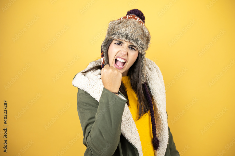 Young beautiful woman wearing a hat and a green winter coat over yellow ...