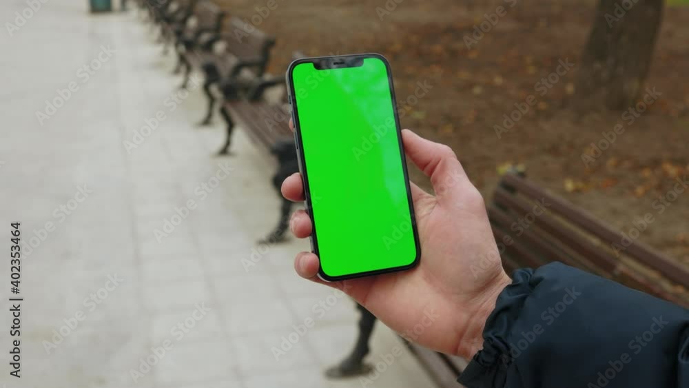 Outdoor man young hand holding use phone with vertical green screen in park background bench ...