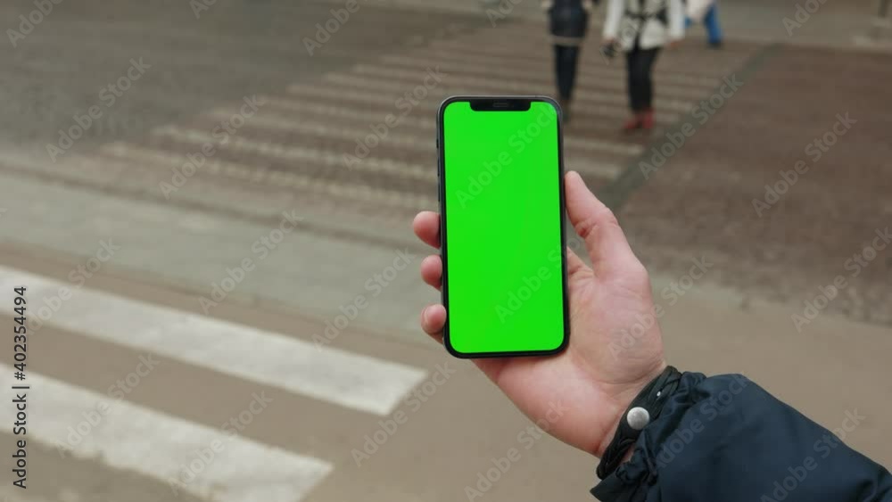 Close up man hand using and tapping phone with vertical green screen on blurred background ...