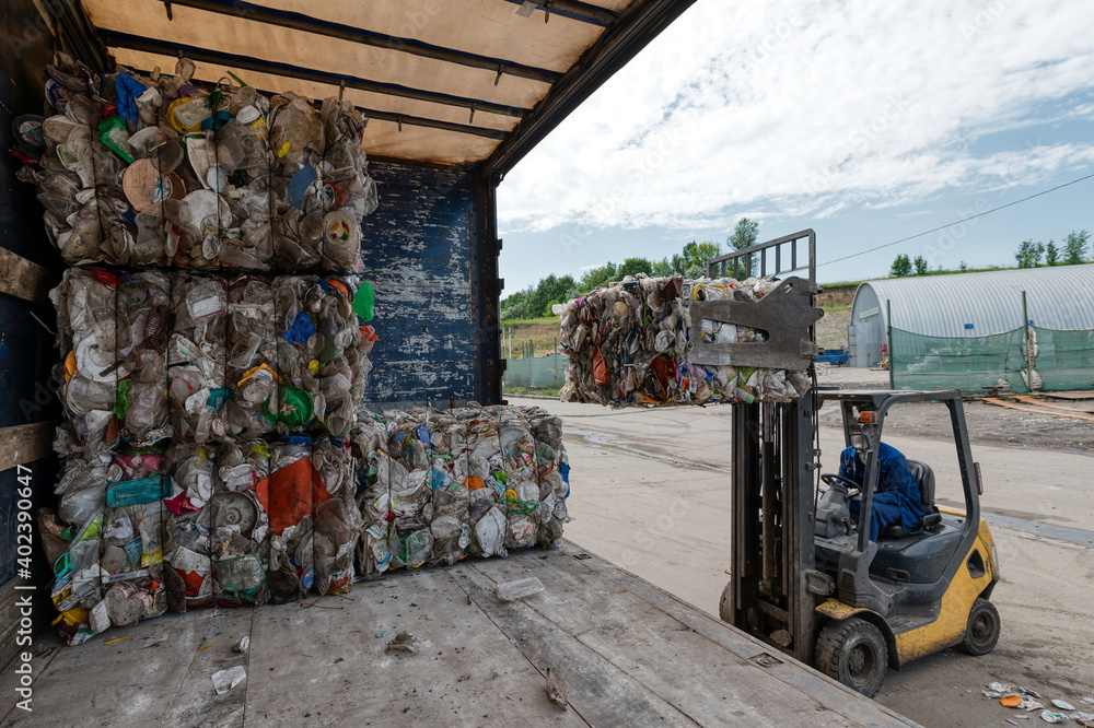 A forklift loads bales of compressed plastic bottles into a truck ...