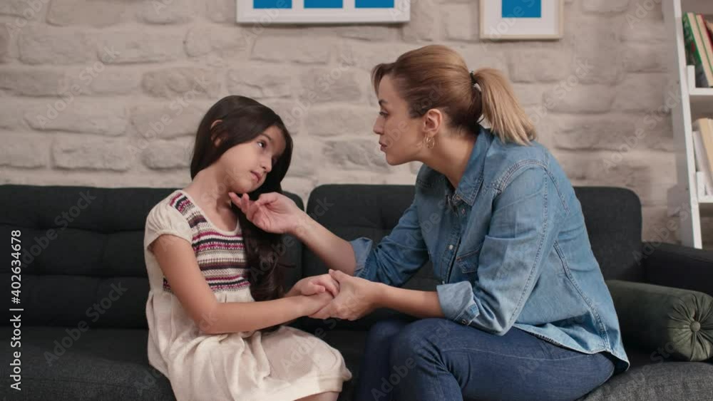 Little cute girl talking to her mother sitting on sofa at home.Loving ...