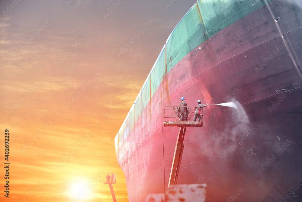 Worker in dry dock with water jet cleaners the side shell hull of the ...