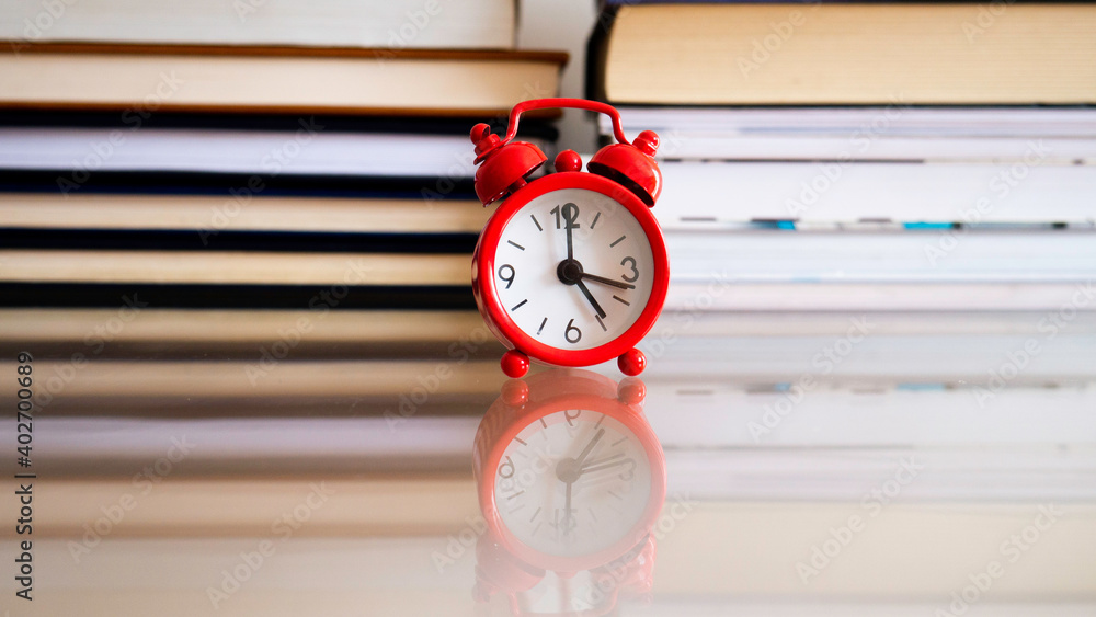 A red clock on a glass table with its reflection and background of a ...