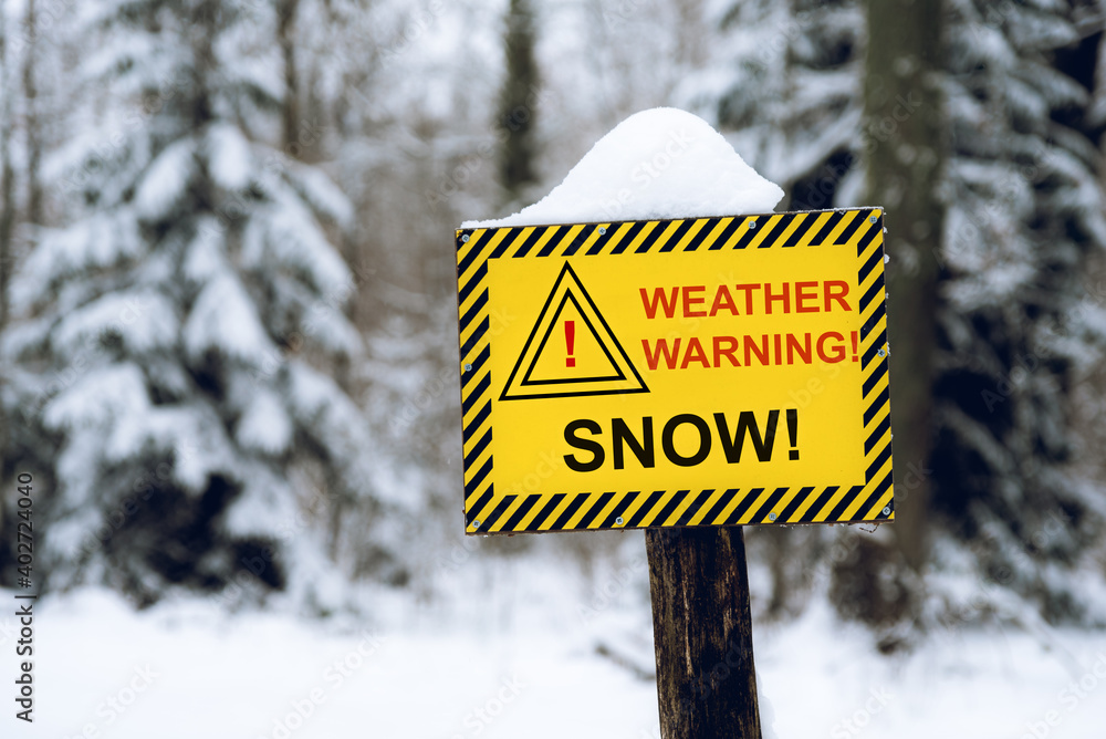 Yellow weather warning snow sign in the out of focus forest background ...