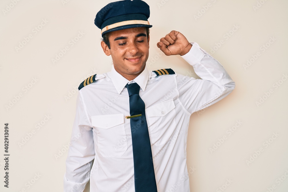 Young hispanic man wearing airplane pilot uniform stretching back ...