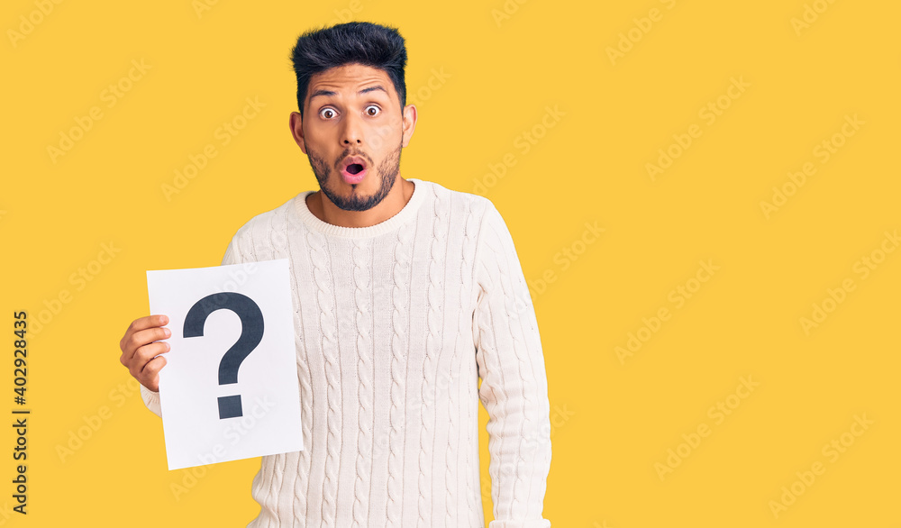 Handsome latin american young man holding question mark scared and ...