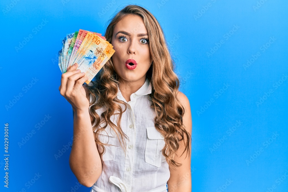 Young blonde girl holding swiss franc banknotes scared and amazed with ...