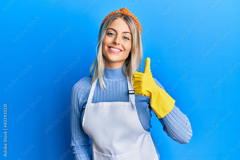 Beautiful blonde woman wearing cleaner apron and gloves doing happy ...