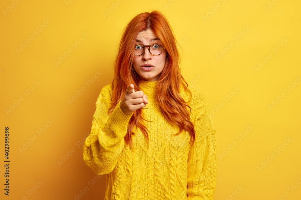 Redhead European woman indicates at you with index finger feels shocked ...
