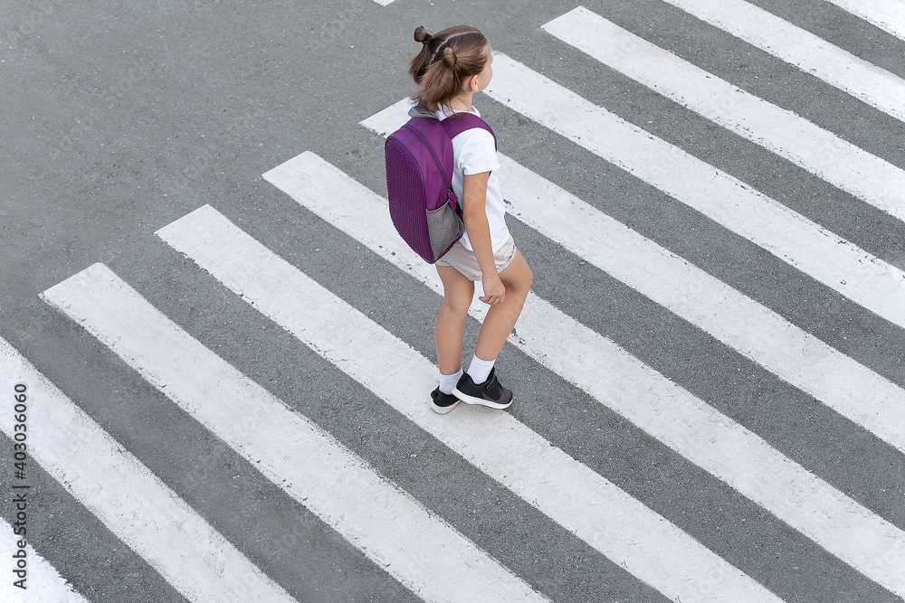 Schoolgirl crossing road on way to school. Zebra traffic walk way in ...