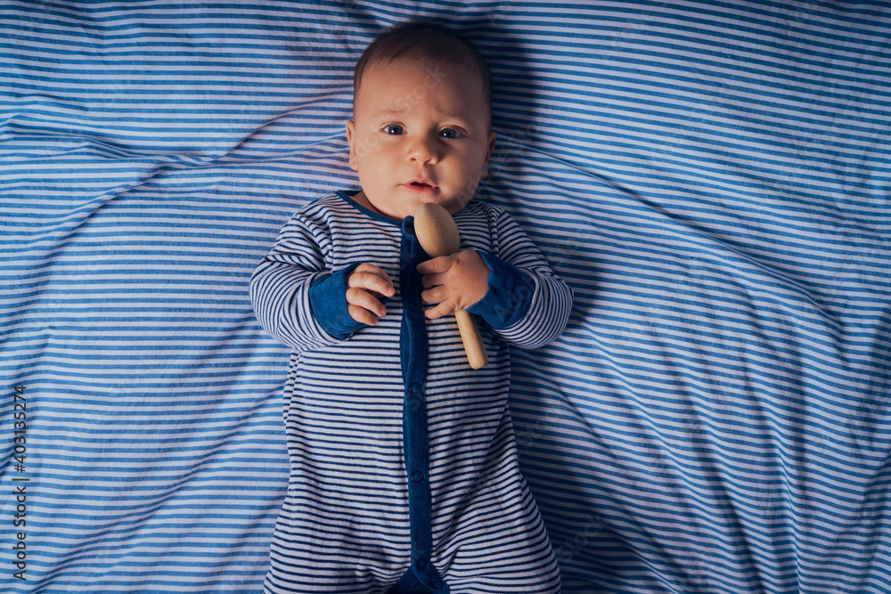 Little baby lying on bed with a wooden rattle Stock Photo | Adobe Stock