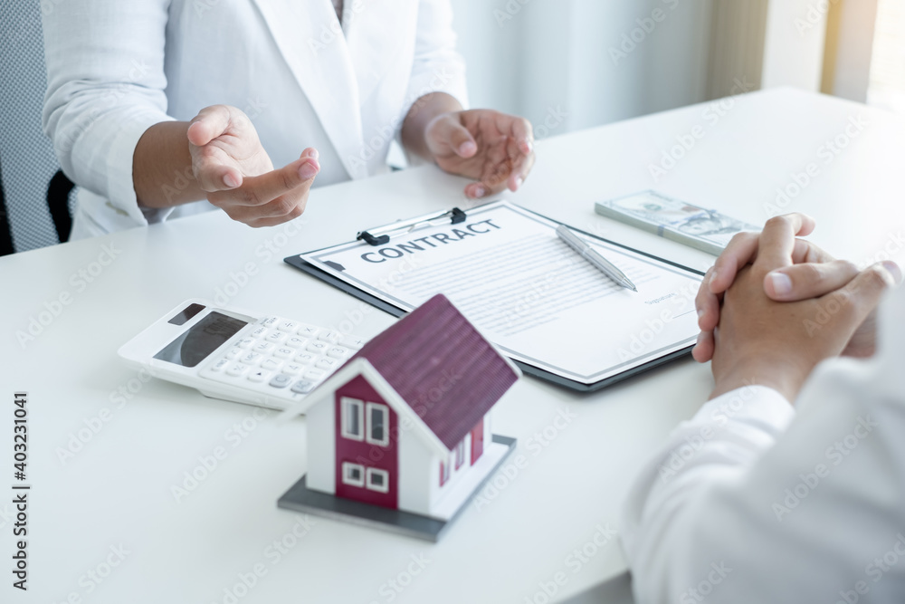 A real estate agent with a House model is talking to clients about ...