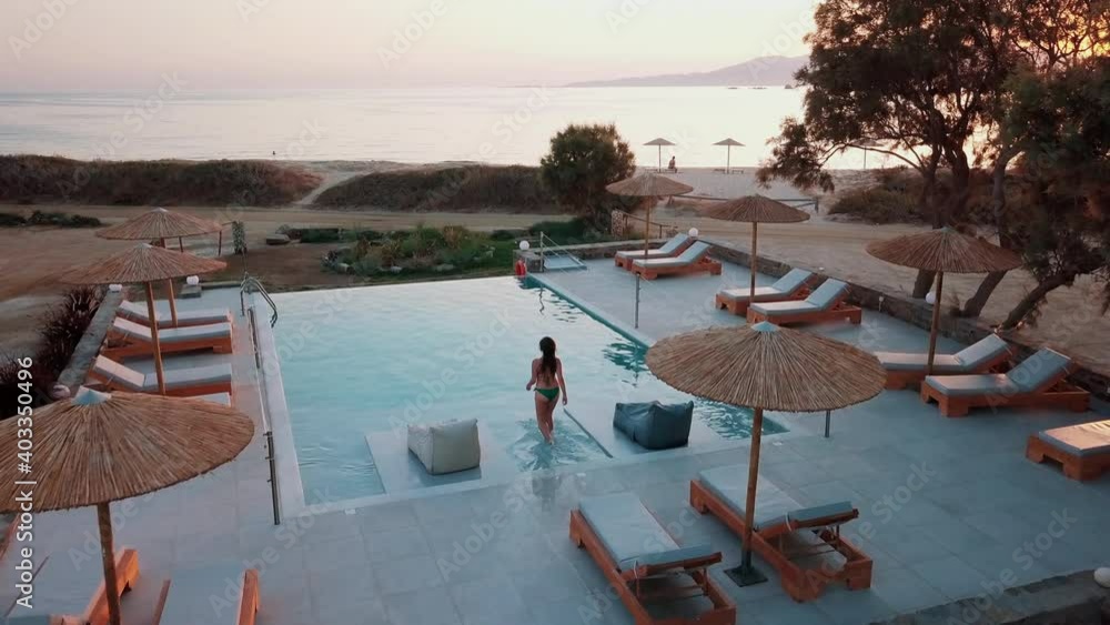 Woman in a bikini stepping into a swimming pool near a beach aerial ...