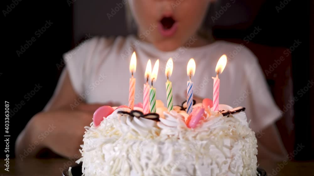 Little smiling child girl blowing birthday celebration sweet cake in dark at home. Blowing ...