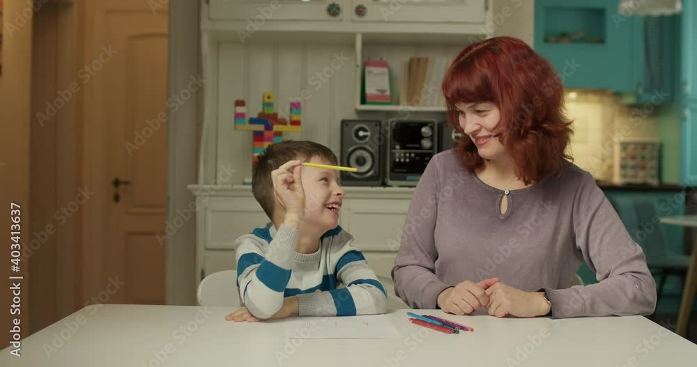 Autistic kid painting with color pencils with mother helping him ...