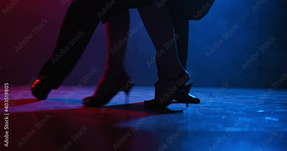 Silhouette of tango dancers feet in a dark room with blue and red ...
