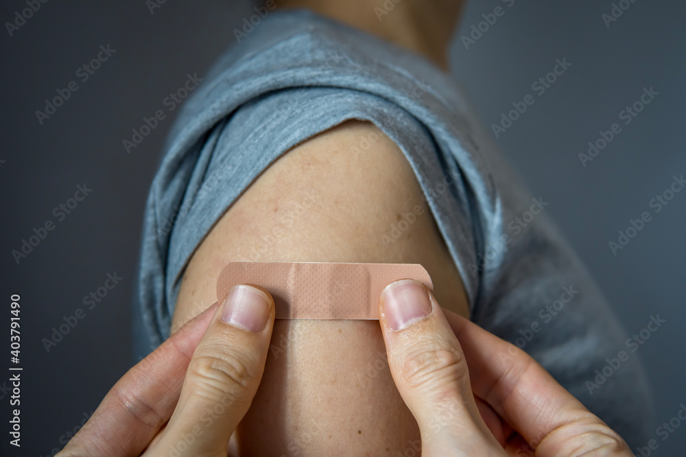 A hand putting an adhesive bandage on a woman's arm after injection of ...