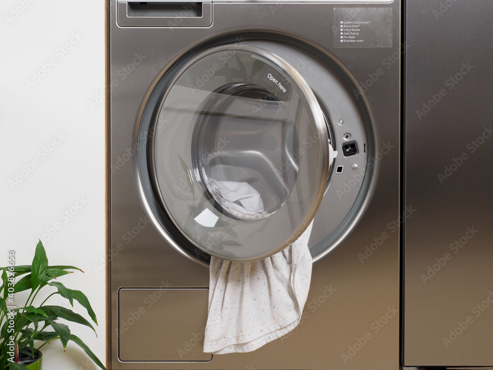 Open door of the washing machine. Clean, light-colored clothes hang out ...