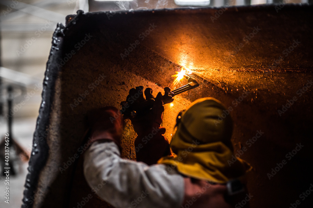 Demolition construction worker using a flame torch to cut up heavy ...