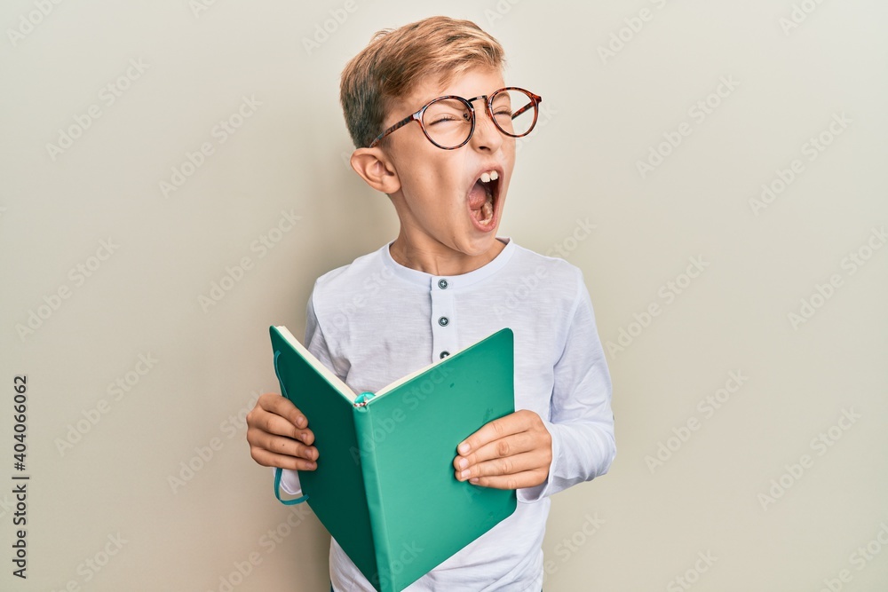 Little caucasian boy kid reading a book wearing glasses angry and mad ...