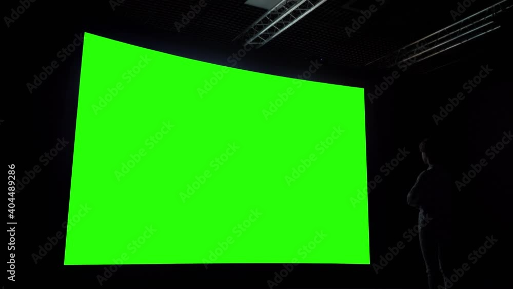 Woman looking at large wall blank interactive green display in dark ...