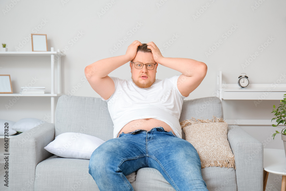 Stressed overweight man in tight jeans at home. Weight loss concept ...