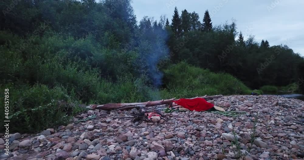 girl in a red cloak is sleeping by the fire. fire is burning, the smoke ...