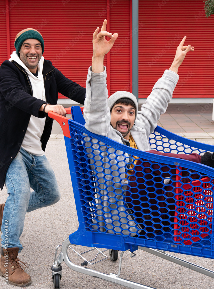 two white caucasian men playing riding in a shopping cart jumping in a ...