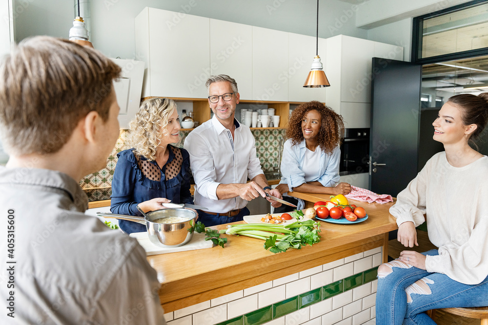 Smiling business colleagues talking while cooking in office kitchen ...