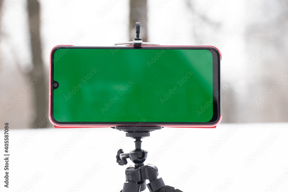 mobile phone with a green screen in winter stands on a flexible stand ...