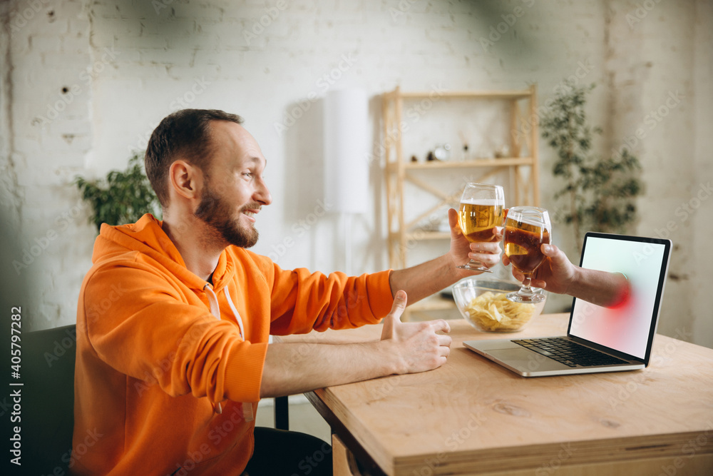 Clinking. Young man drinking beer during meeting friends on virtual ...