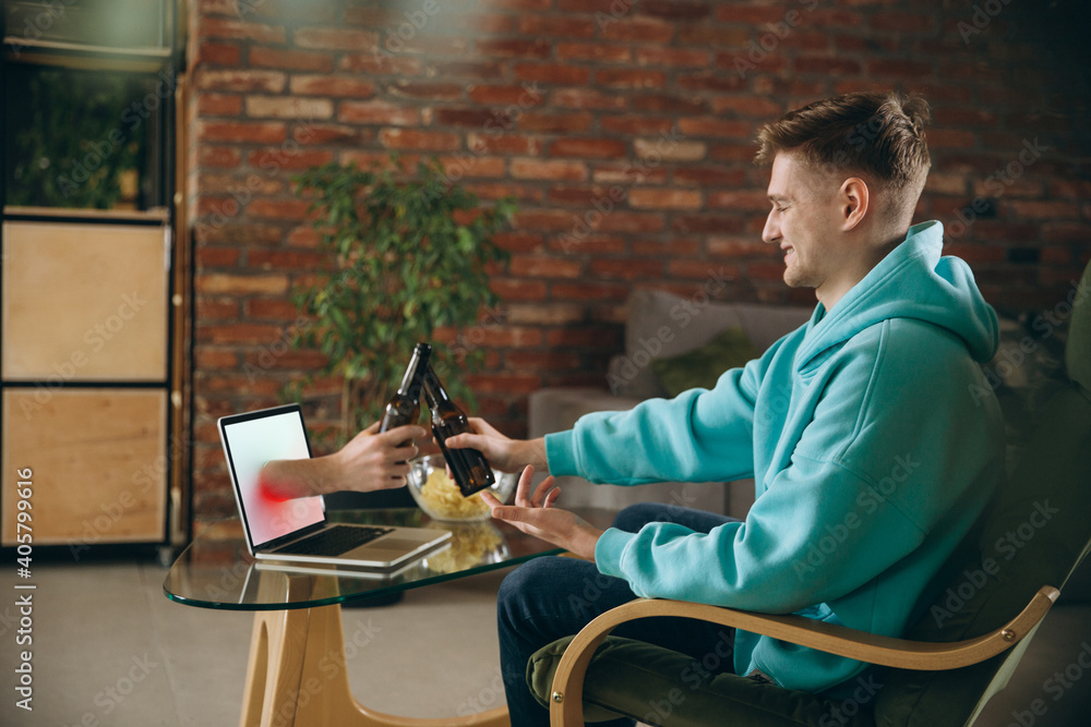 Clinking. Young man drinking beer during meeting friends on virtual ...