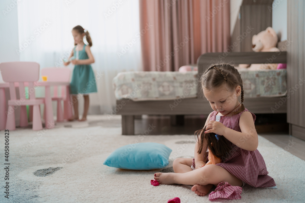 Cute little girl playing with a doll whille sitting on the carpet in ...