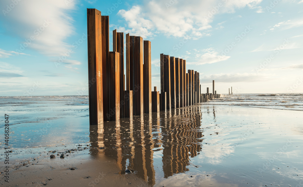 Large rusty steel construction pillars in the sand on a sunny beach ...